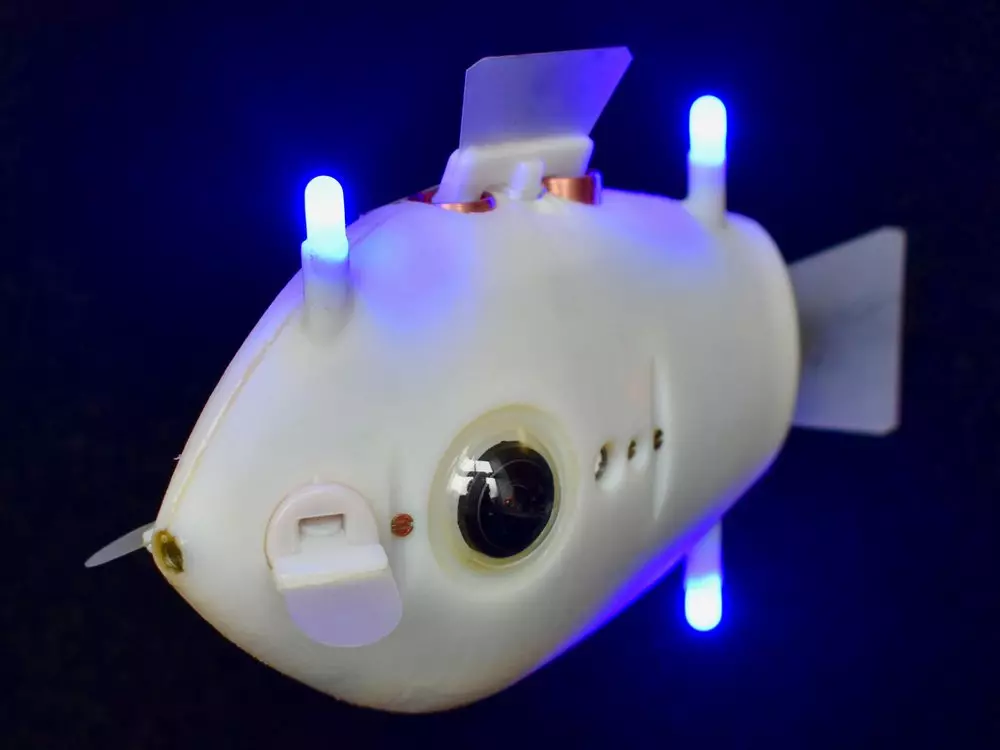 Снимка на бяла роботизирана риба на черен фон. Роботът има два светодиода отгоре и един отдолу