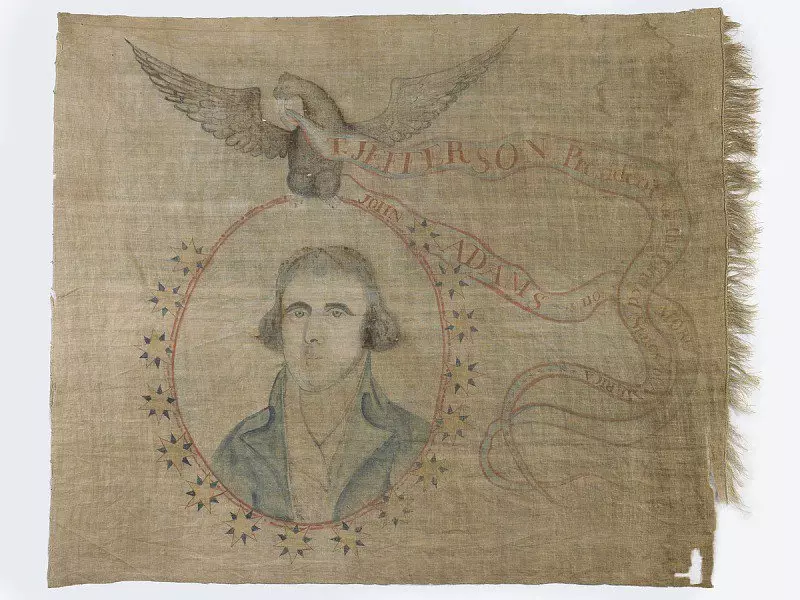 Obledela platnena pasica, obrabljena na robovih, s portretom Jeffersona, obkroženim s cvetličnim vencem, in orlom nad glavo