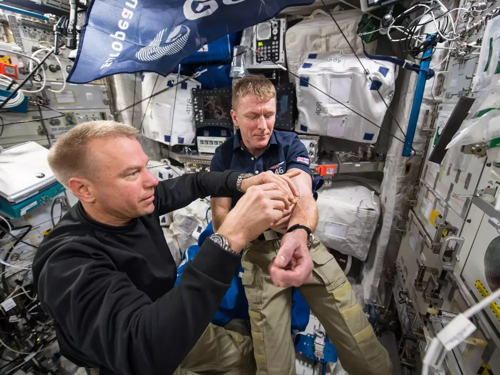 Un astronaut masculin de la NASA Tim Kopra efectuează extragerea de sânge pe astronautul Agenției Spațiale Europene Tim Peake pe stația spațială internațională