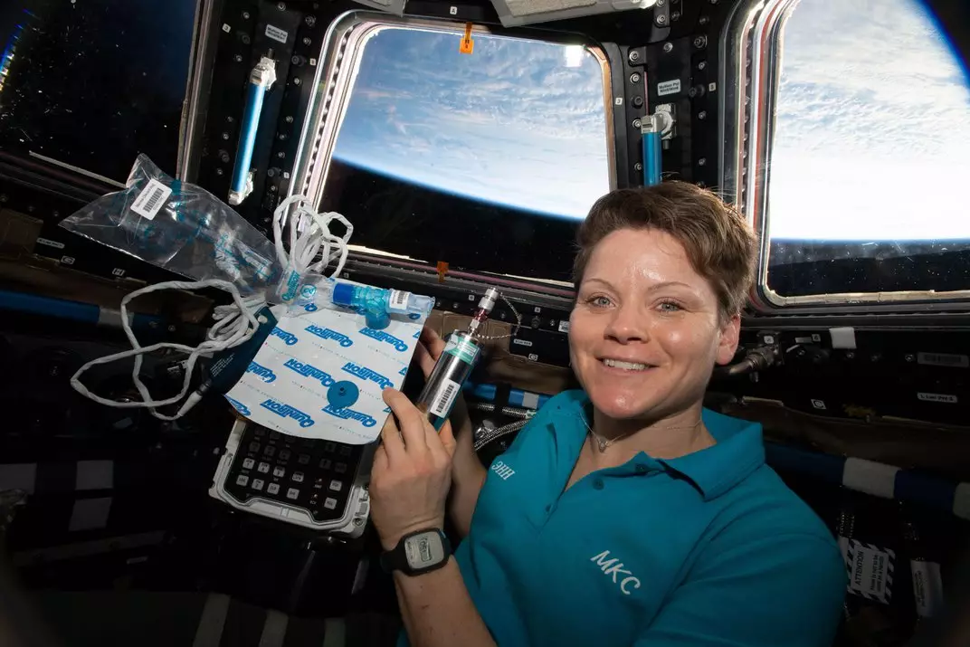 Femeie astronaută Anne McClain ținând echipament biomedical pentru studiu în timp ce se afla pe Stația Spațială Internațională.