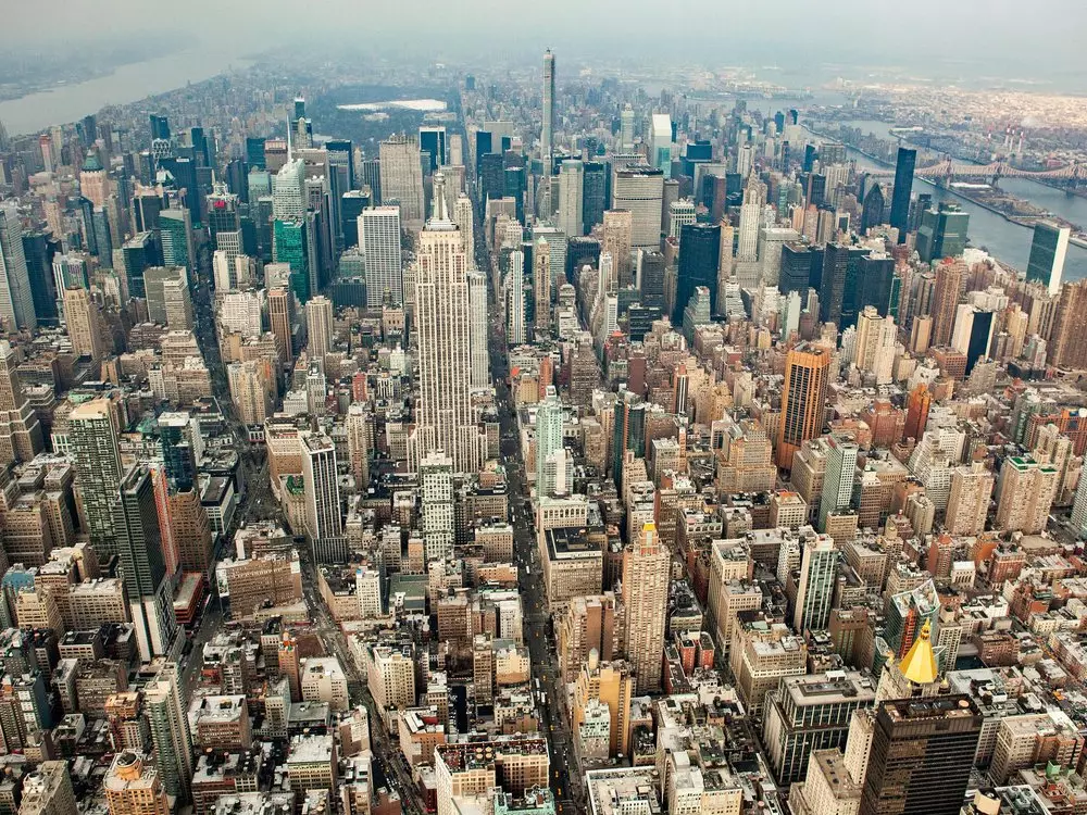 न्यूयॉर्क शहराचे हवाई छायाचित्र. क्षितिजापर्यंत पसरलेल्या गगनचुंबी इमारती आणि चमकदार इमारतींच्या अंतहीन पंक्ती आहेत.