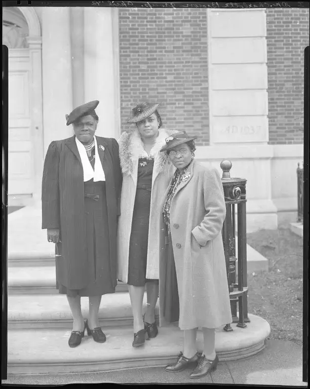 'n Swart-en-wit foto van drie Afro-Amerikaanse vroue wat op die trappe van 'n gebou staan. Hulle dra almal jasse, hoede, borsels en kouse. Die vrou heel links staar vasberaden in die kamera af.