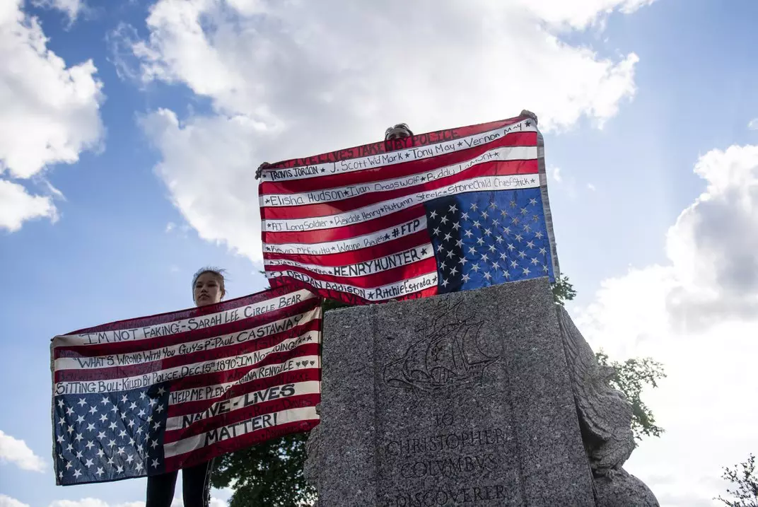 Dua aktivis memegang bendera yang memaparkan nama orang asli Amerika yang dibunuh oleh polis.