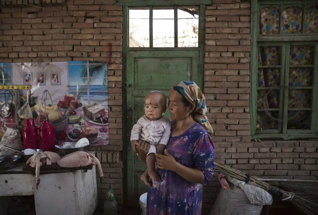 12 ستمبر، 2016 کو کوربن فیسٹیول کے دوران ایک ایغور خاتون اپنے گھر میں کھانا تیار کرتے ہوئے بچے کو اٹھائے ہوئے ہے۔