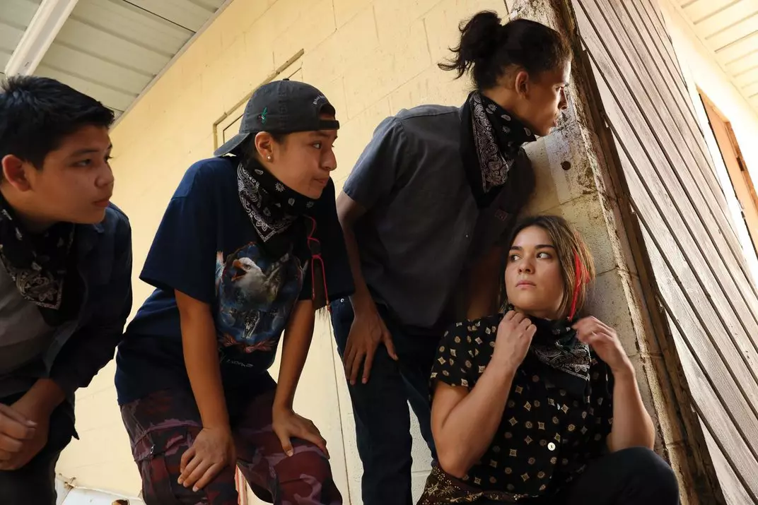 drei Teenager der amerikanischen Ureinwohner, die um eine Wand spähen, und ein Teenager-Mädchen der Ureinwohner, das zu ihnen zurückblickt