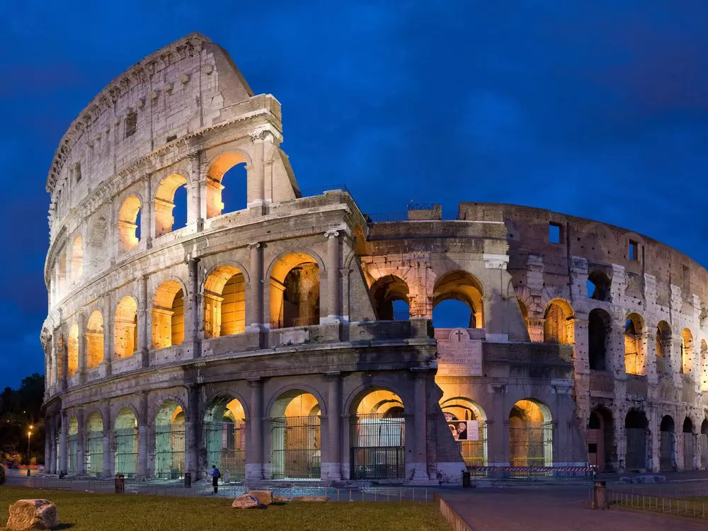 A Colosseum éjszaka, kék égbolttal és sárga fénnyel megvilágított boltíveivel. A szerkezet részben lebontott, falainak fele lebontva