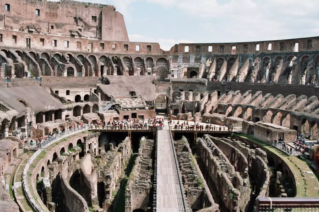 O vedere aeriană a interiorului Colosseumului, cu ziduri arcuite de jur împrejur; pe sub locul unde era podeaua, o rețea de arcade și tuneluri se întinde mult sub pământ