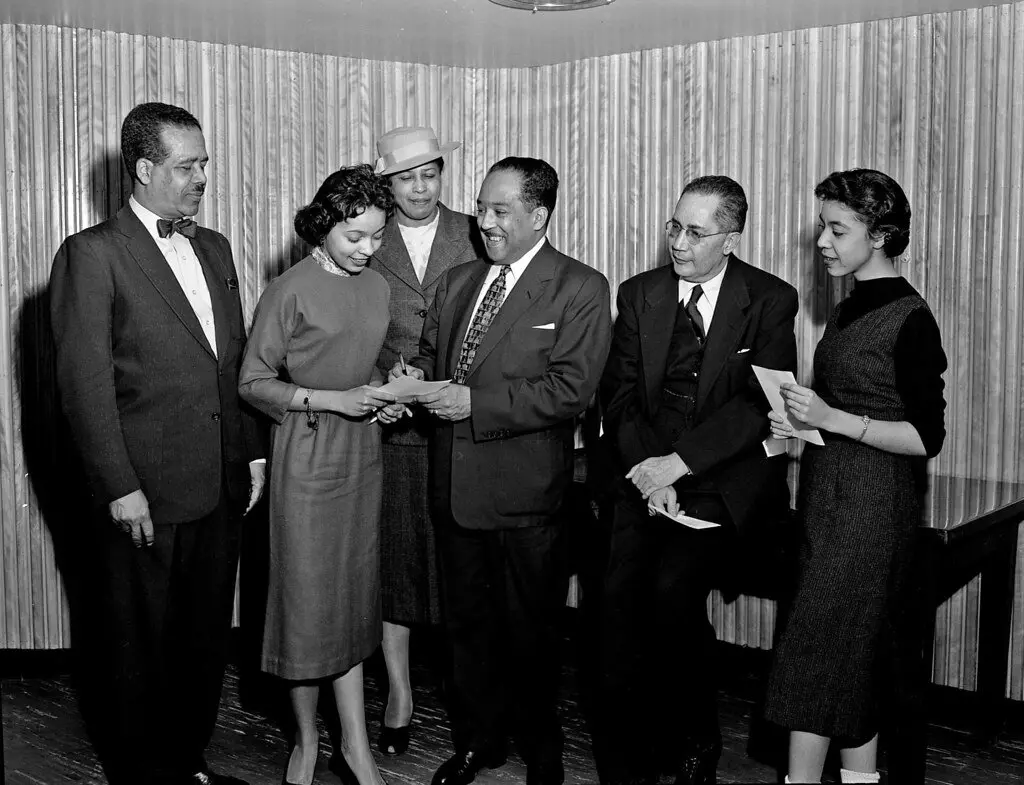 swart-en-wit foto van formeel geklede swart mans en vroue saam met Langston Hughes