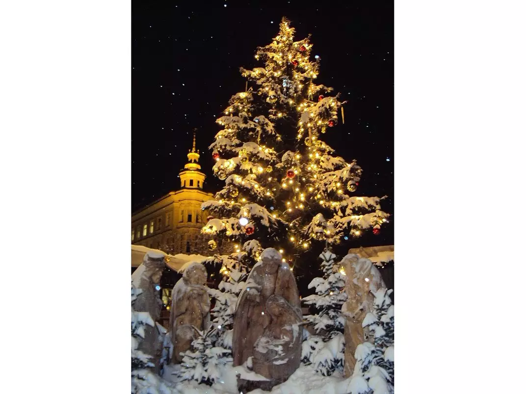 A imponente árvore de Natal se iluminou, atrás de estátuas de anjos cobertas de neve.