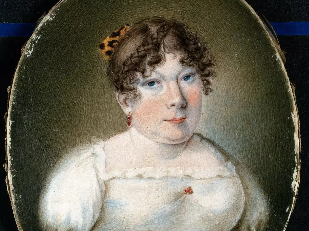 Un retrato en miniatura dunha muller branca de pelo castaño rizado cun vestido branco de emperatriz cunha cinta azul; os seus brazos rematan por debaixo do ombreiro, onde está fixado o seu vestido
