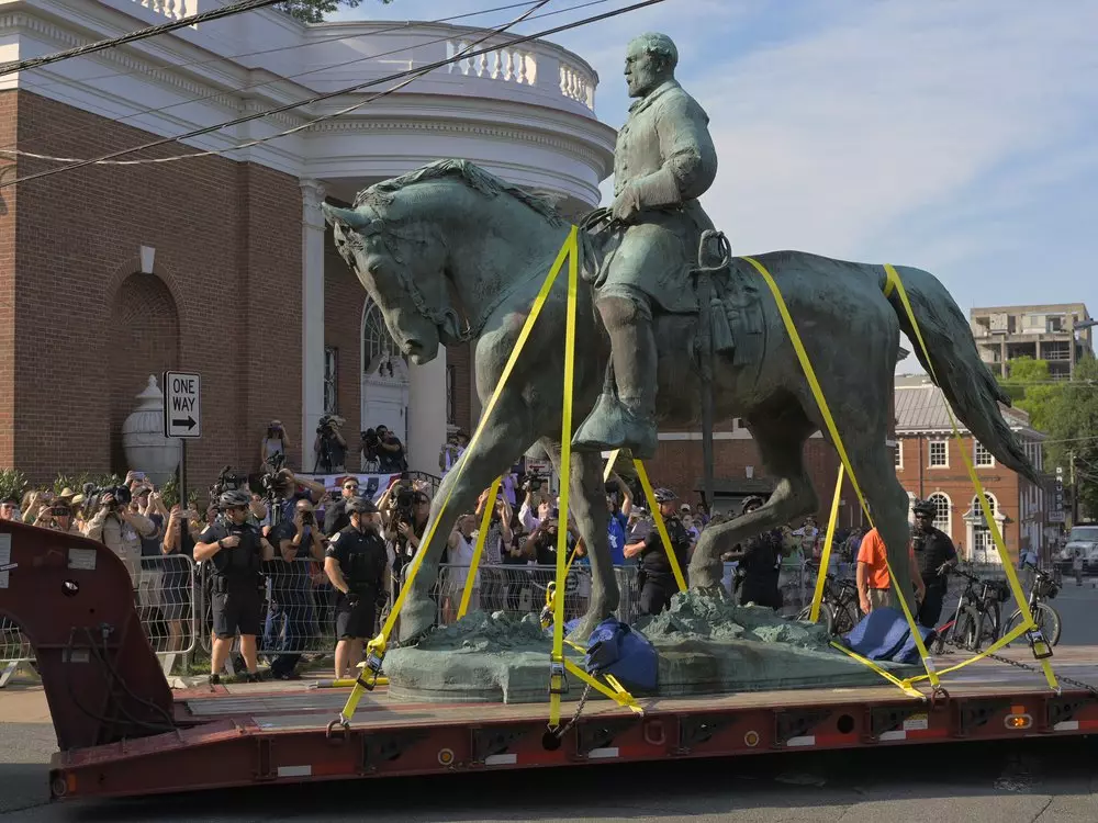 Các đội xây dựng vận chuyển một bức tượng bằng đồng màu xanh lục của Lee trên lưng ngựa băng qua đám đông người xem trên một chiếc xe tải giường nằm