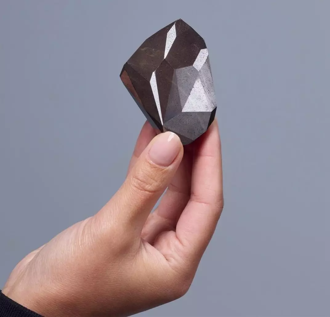 Een hand met een geslepen zwarte diamant ter grootte van een kleine peer